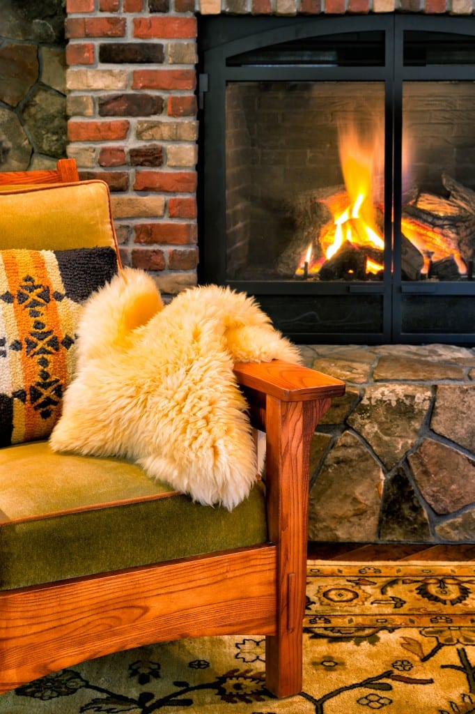 Chair by a stone and brick fireplace with a crackling fire. Cozy ...